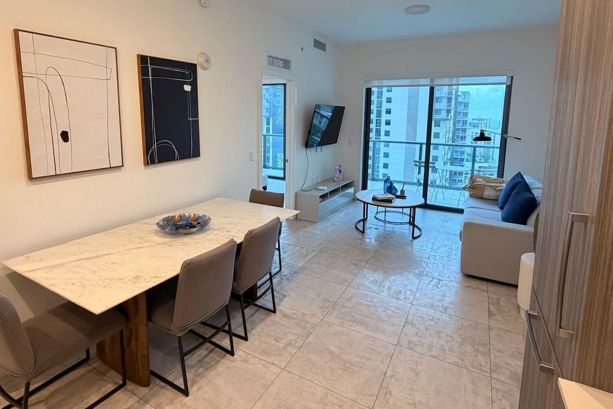 Um apartamento moderno com área de jantar, sala de estar e uma grande janela com vista para a cidade.