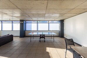 Um quarto espaçoso com uma mesa grande, cadeiras e teto alto.
