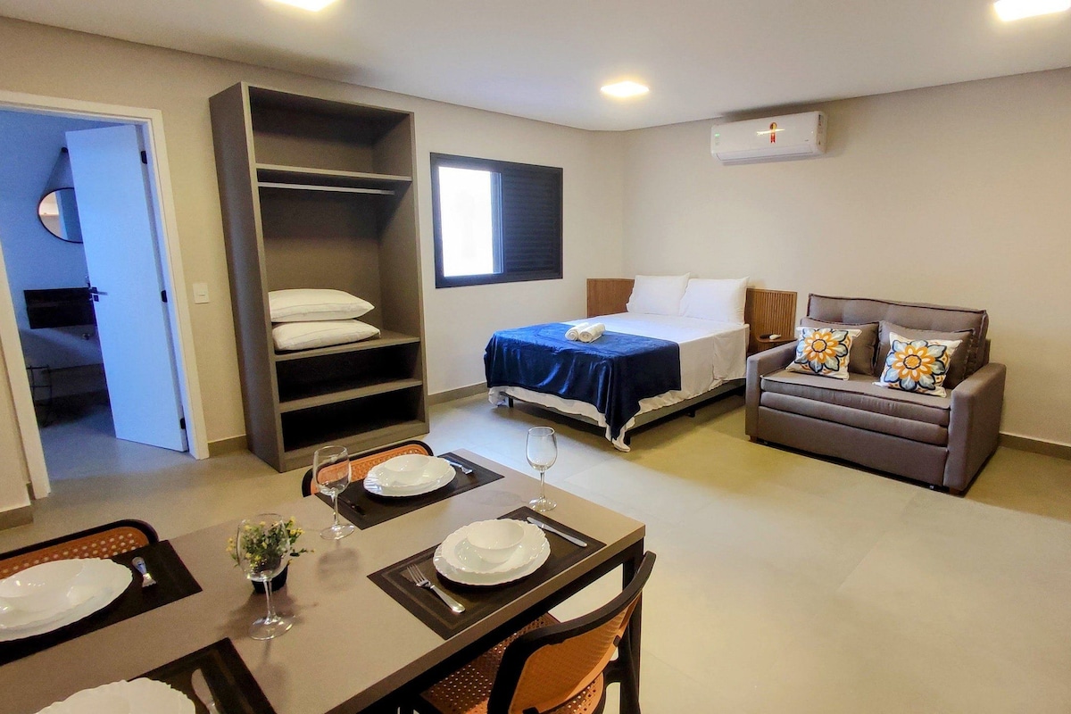 Quarto de hotel com cama, sofá, mesa de jantar posta para dois e closet espaçoso.
