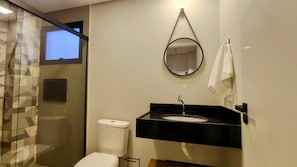 Um banheiro com box de vidro, vaso sanitário, pia com bancada preta e espelho com uma toalha pendurada na parede.