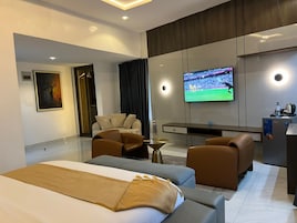Quarto de hotel moderno com uma cama grande, dois sofás, uma pequena mesa, uma TV e um minibar.