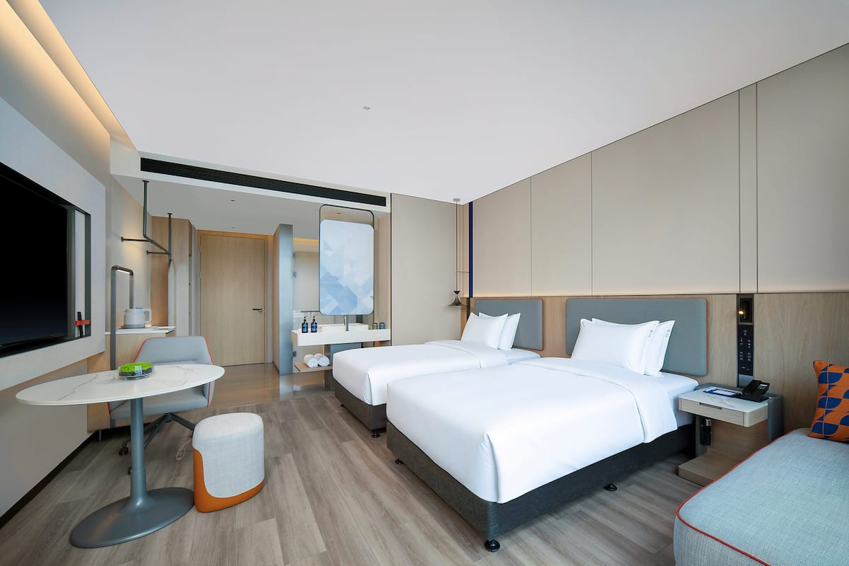 Quarto de hotel moderno com uma cama grande, uma escrivaninha, uma cadeira e uma televisão.