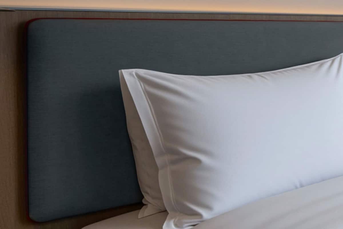 Cama com cabeceira cinza e travesseiros brancos.