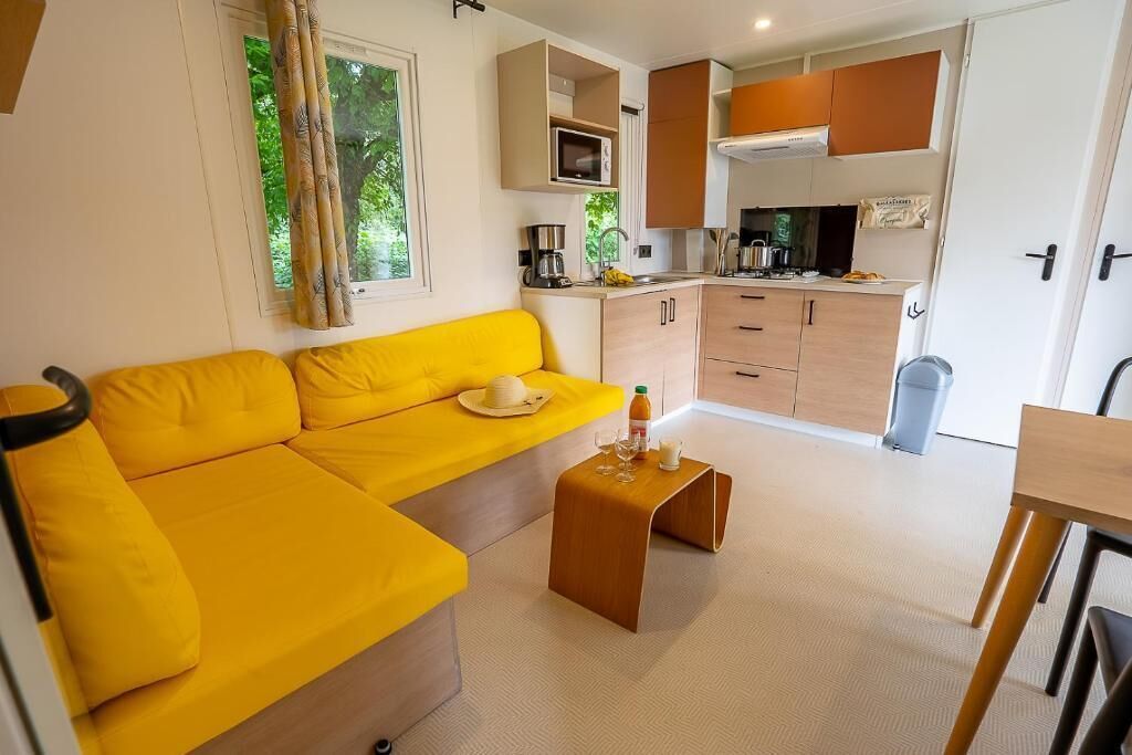 Um espaço de estar compacto com um sofá amarelo, uma pequena mesa de madeira e uma cozinha compacta.