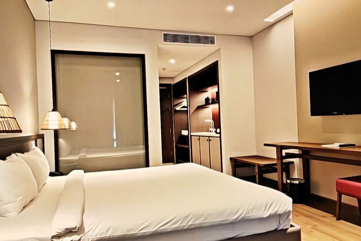Quarto de hotel com cama, escrivaninha, televisão e armário.