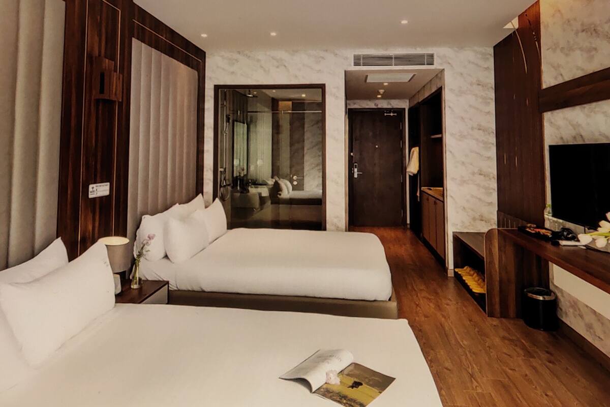Quarto de hotel com uma cama grande, uma mesinha de cabeceira, uma televisão e um espelho.