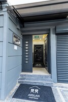 Entrada de um edifício com porta numerada, placa indicando 'ARSLAN APARTMANI' e tapete de entrada com o mesmo nome.