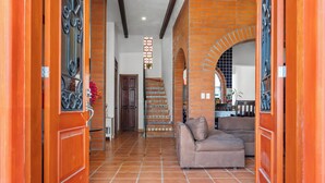 Uma sala de estar ampla com sofá, escada com azulejos estampados e porta de madeira.
