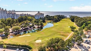 Campo de golfe com lago, rodeado por árvores e um parque de estacionamento.