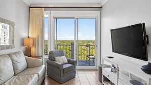 Quarto com sofá, poltrona listrada, televisão e varanda com vista.