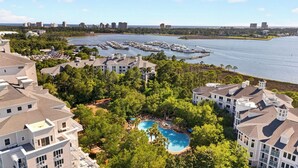 Área residencial com piscina rodeada por árvores, marina com barcos e o horizonte urbano ao fundo.