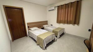 Quarto de hotel com duas camas, uma porta de madeira, aparelho de ar condicionado e cortina.