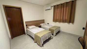 Quarto de hotel com duas camas, uma porta de madeira, aparelho de ar condicionado e cortina.