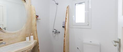 Uma casa de banho com lavatório, espelho, chuveiro e sanita.