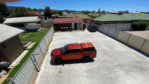 Uma área de estacionamento com um SUV vermelho, edifícios cercados e céu claro.
