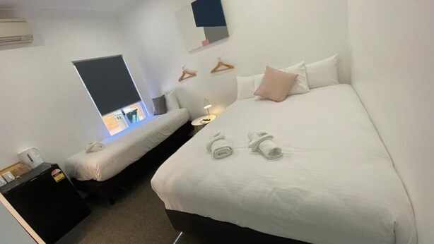 Quarto de hotel com uma cama grande, uma cama menor, uma escrivaninha com abajur e uma televisão na parede.