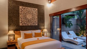 Quarto de hotel com uma cama, duas luminárias de cabeceira, um detalhe decorativo na parede e uma porta de vidro deslizante para uma área externa com cadeiras de descanso.