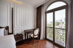 Quarto de hotel com cama, escrivaninha, cadeira, telefone e varanda com vista para edifícios.