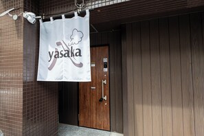 Entrada de um edifício com uma faixa pendurada contendo a palavra 'yasaka' e uma porta de madeira.