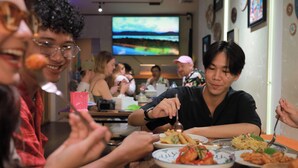 Um grupo de pessoas jantando em um restaurante, com uma televisão ao fundo.