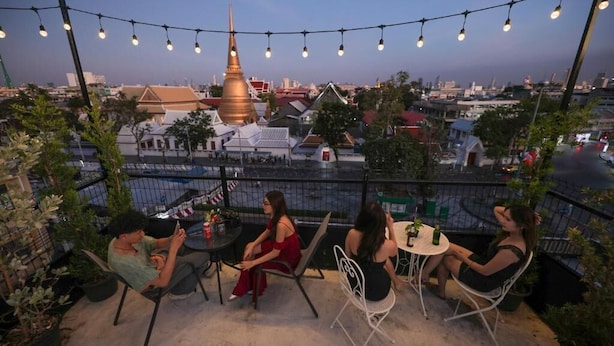 Terraço no telhado com luzes de festa, vista para a paisagem urbana e uma torre dourada ao fundo.