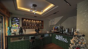 Uma área de bar com balcão revestido de azulejos verdes, banquetas, uma árvore de Natal e uma placa com a inscrição 'Bud Brew & Beyond'.