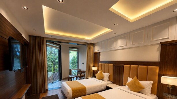 Quarto de hotel com duas camas, televisão, secretária e varanda com cortinas.