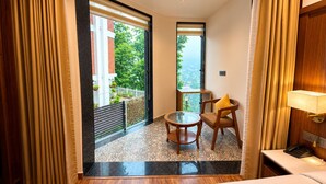 Quarto de hotel com cama, mesinha, cadeira, mesa de cabeceira e vista para o exterior.