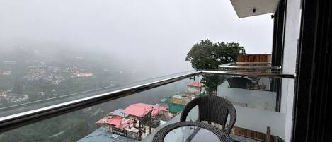 Uma varanda com mesa e cadeiras de vidro, com vista para prédios e uma árvore.