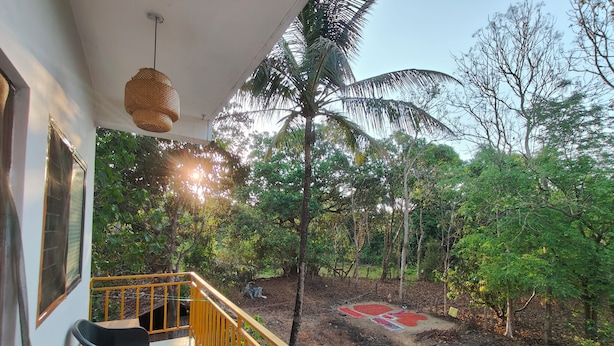Uma varanda com guarda-corpo amarelo, uma cadeira de plástico e um lustre suspenso.