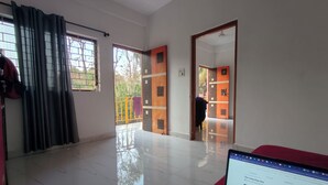 Um quarto amplo com uma janela grande, um laptop em um sofá vermelho e uma porta de madeira que dá para outro quarto.