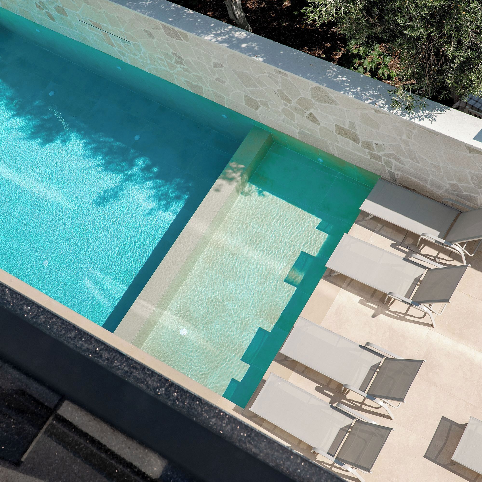 Piscina translúcida com paredes de pedra e espreguiçadeiras.