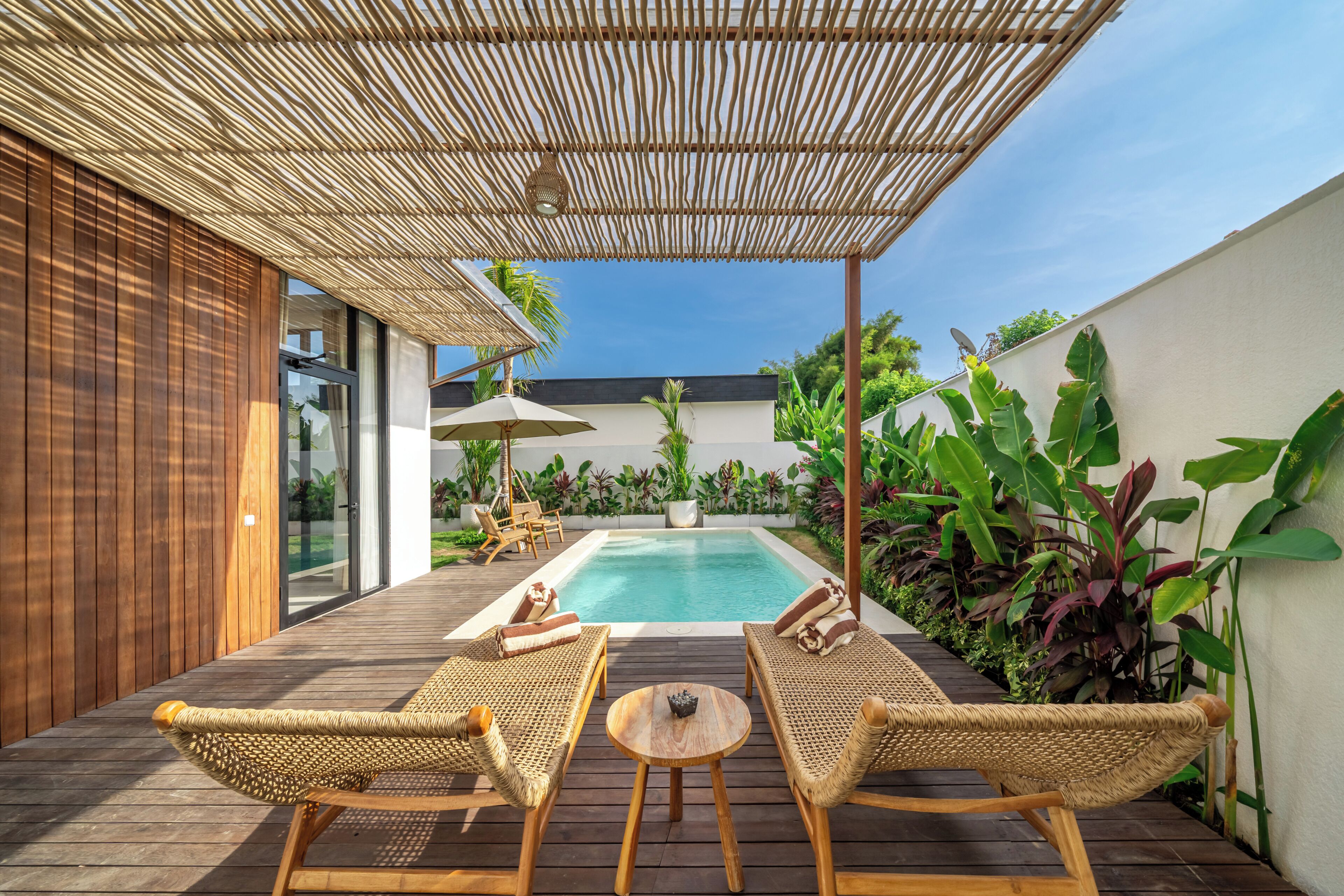 Um deck de madeira com duas cadeiras de vime, uma mesa redonda pequena e uma piscina.