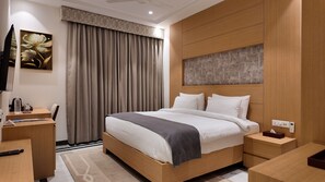 Quarto de hotel moderno com cama de madeira, uma escrivaninha, uma cadeira, televisão de tela plana e uma janela grande com cortinas.