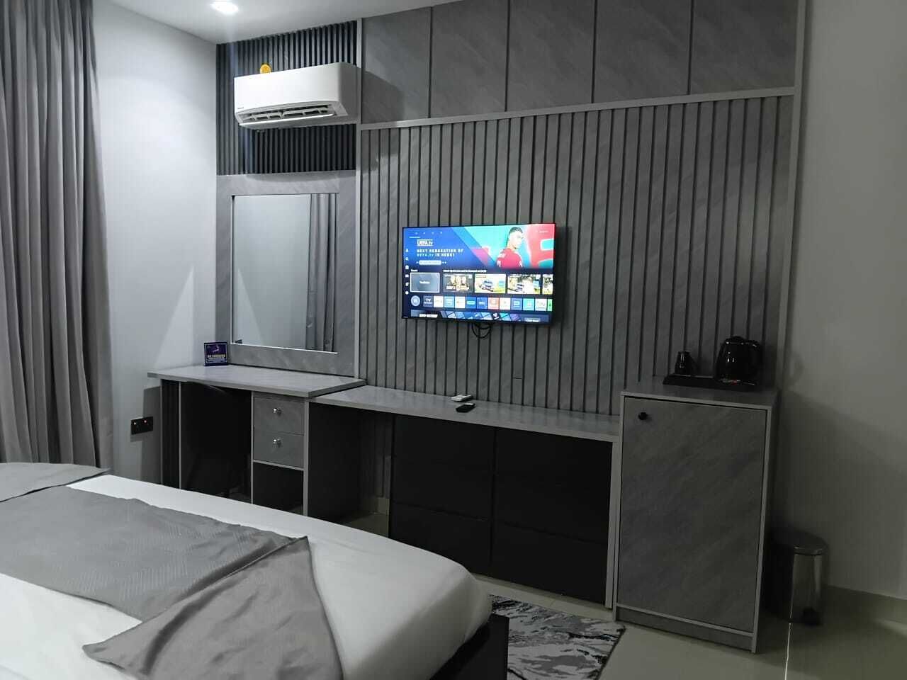 Quarto de hotel moderno com uma cama, uma escrivaninha com televisão de tela plana, um espelho e um guarda-roupa.