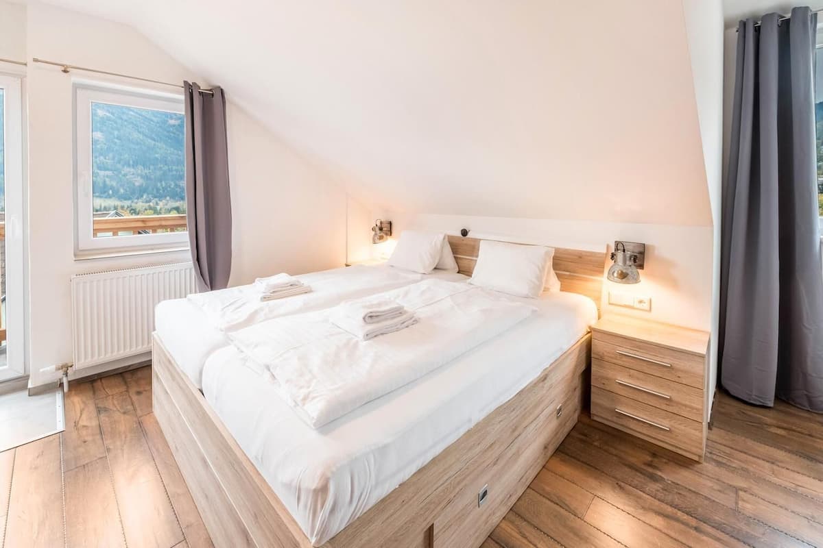 Quarto com cama grande, cabeceira de madeira, mesas de cabeceira e vista para o exterior.