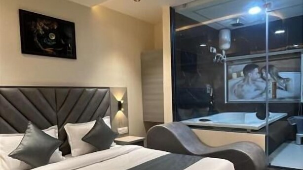 Quarto moderno com cama grande, mesa de cabeceira, TV na parede e janela ampla.
