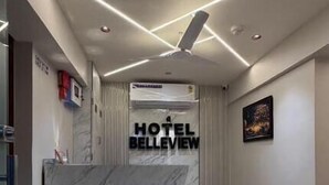 Uma mesa de recepção com a identificação 'RECEPTION' em um hotel chamado 'HOTEL BELLEVIEW', com um ventilador de teto e iluminação embutida.