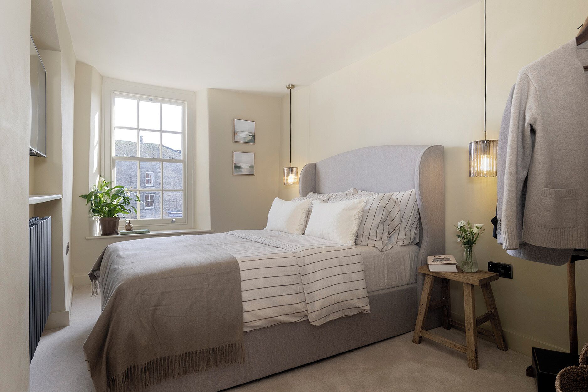 Quarto com cama, janela, mesa de cabeceira e cabides.