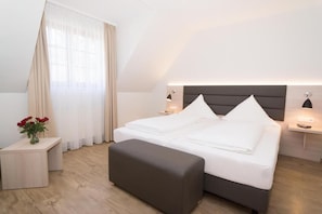 Quarto de hotel moderno com cama, mesas de cabeceira e uma janela com cortinas.