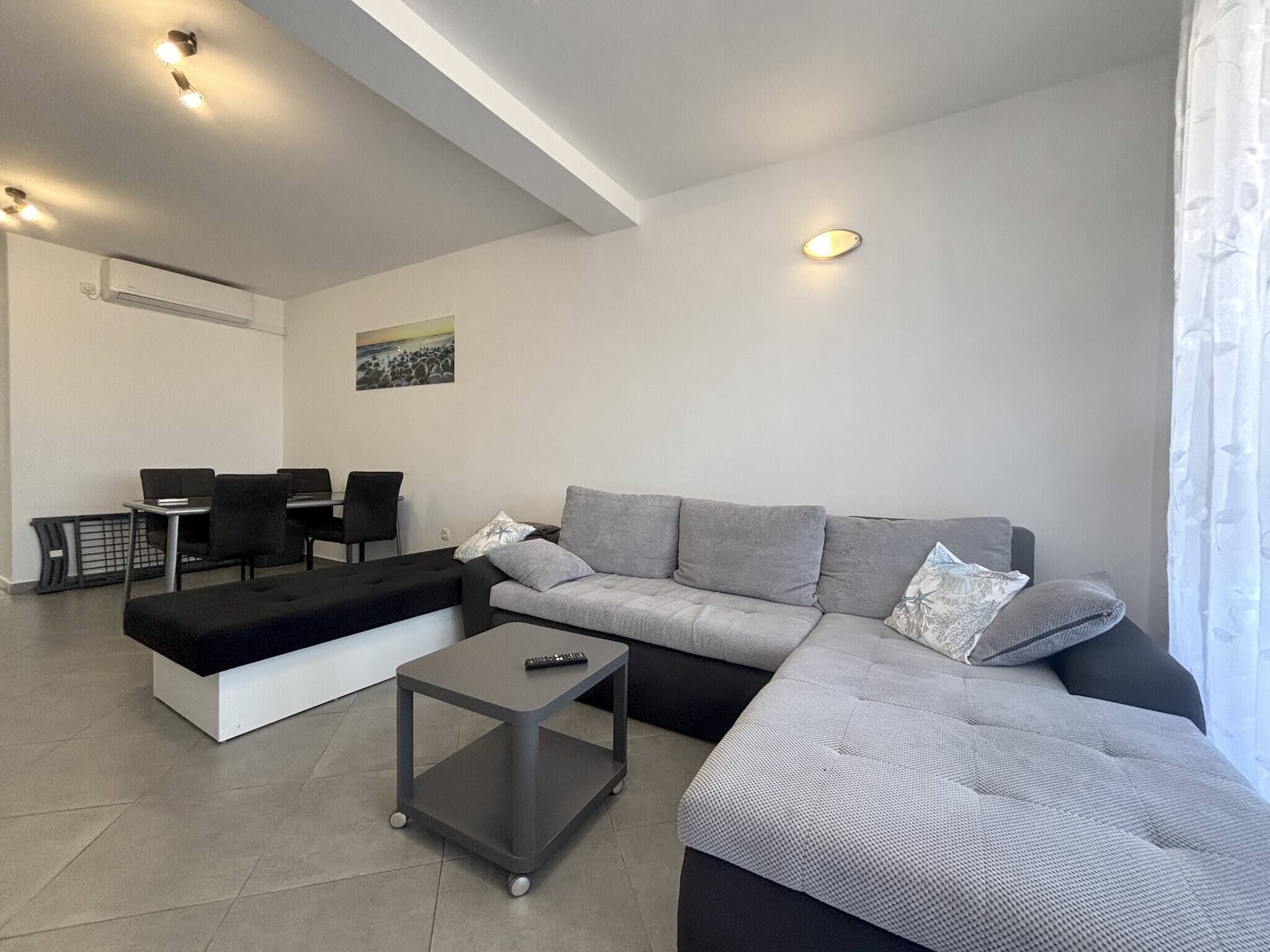 Uma sala de estar moderna com um sofá seccional cinza, uma mesinha de centro e um espaço de jantar com cadeiras e uma mesa.