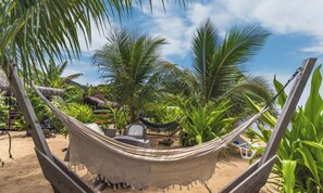 Uma rede em um jardim tropical com uma estrutura de telhado de palha e diversas plantas.