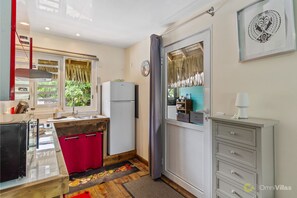 Cozinha compacta com geladeira, pia e janela com cortinas.