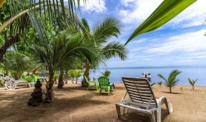 Uma praia com cadeiras de praia, palmeiras e um barco na água.