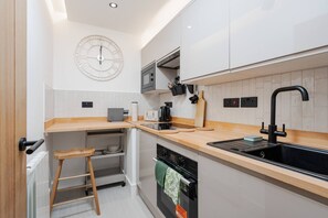 Uma cozinha compacta com bancada de madeira, pia preta, relógio e micro-ondas.