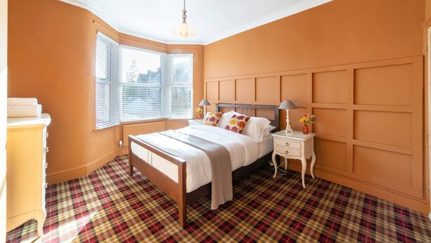 Um quarto com cama, mesas de cabeceira, cômoda, janela com persianas e piso estampado xadrez.