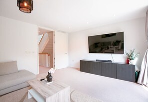 Uma sala de estar moderna com um sofá, uma mesa de centro, uma TV fixada na parede e uma escada que leva a outro cômodo.