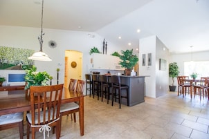 Cozinha moderna com área de jantar, destacando uma ilha central, banquetas de bar e plantas em vasos.