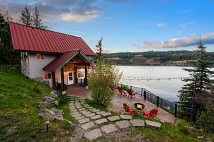 Uma cabana com telhado vermelho, um deck com área de estar externa e vista para um lago.