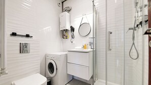 Casa de banho moderna com sanita, máquina de lavar roupa e cabine de duche de vidro.